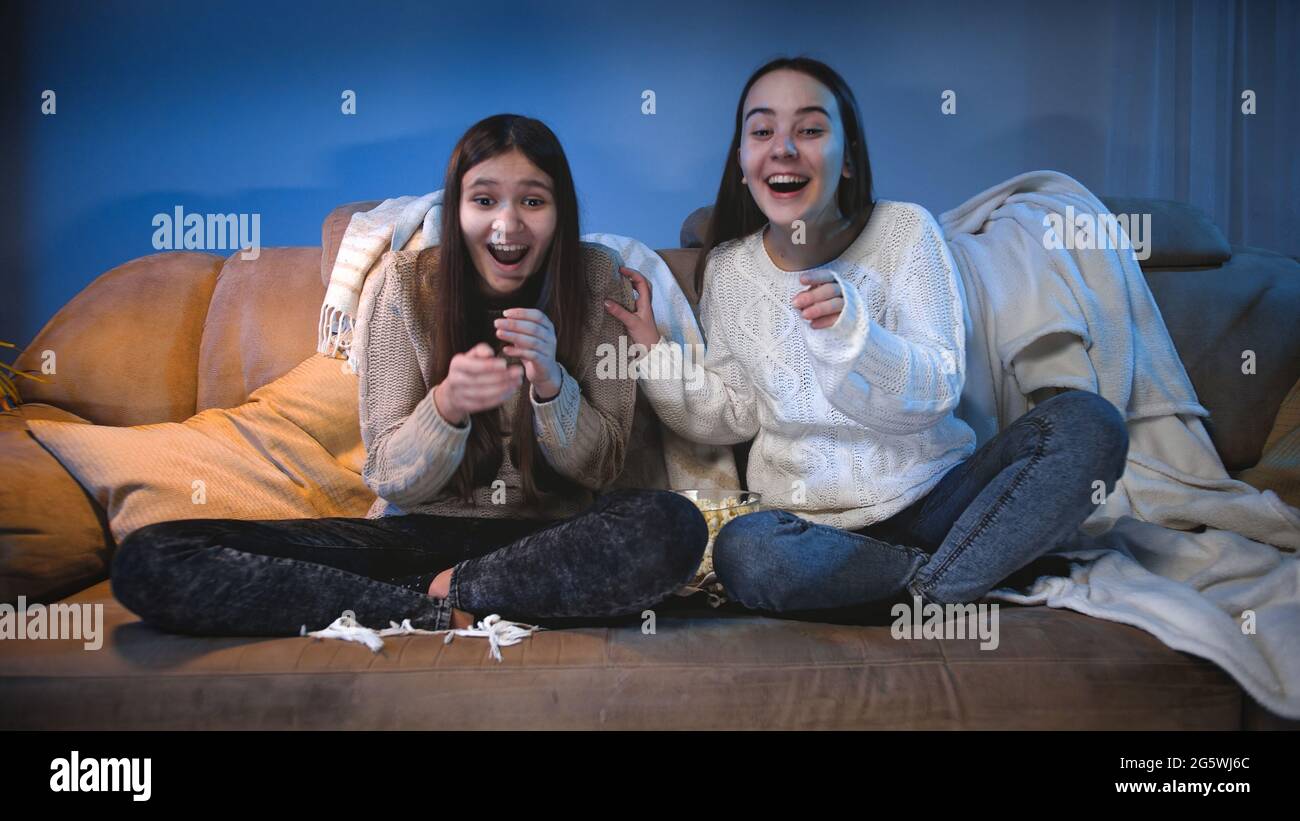 Two smiling girls watching funny movie or TV program and laughing on ...