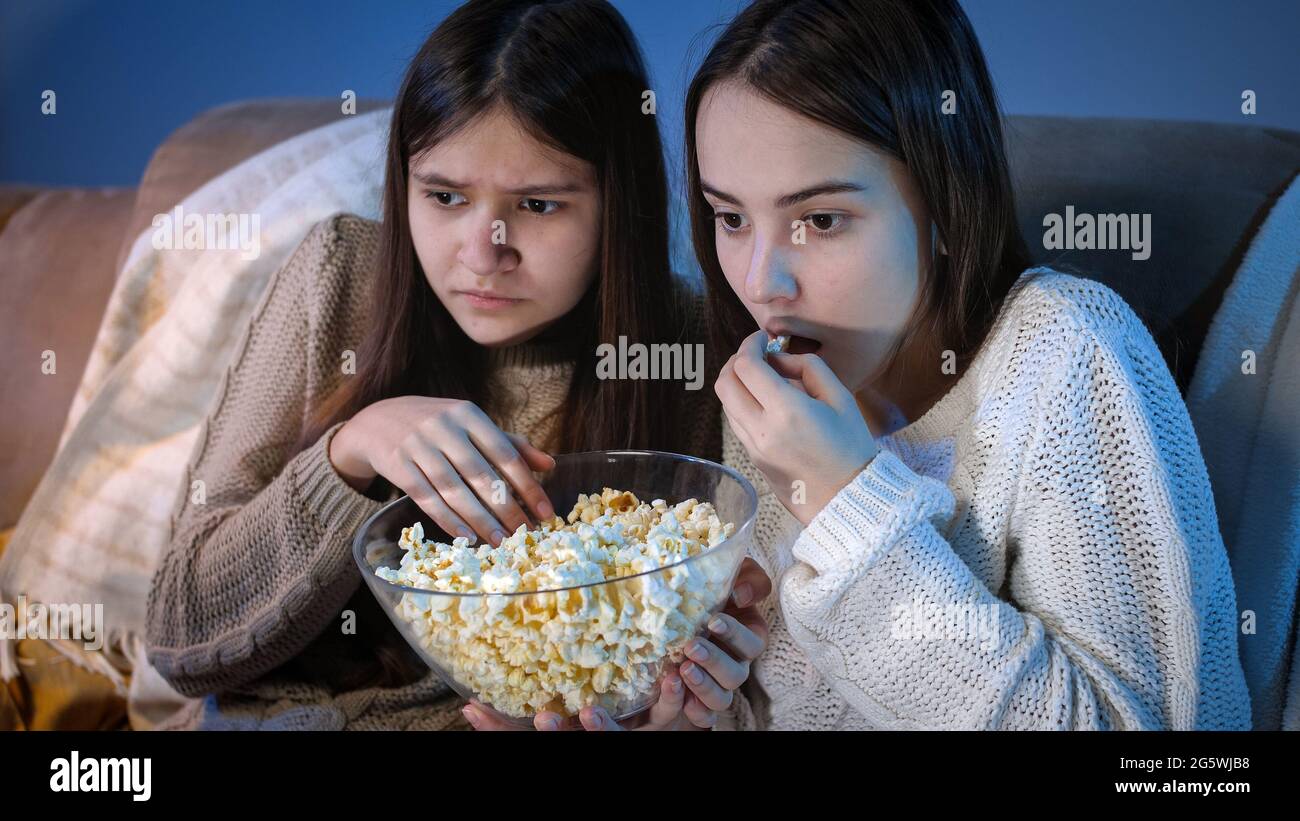 Two girls eating popcorn from big bowl while watching scary horror ...