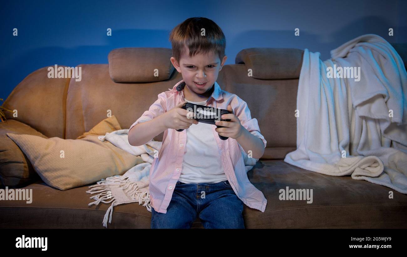 Funny little boy holding game controller while playing video games on ...