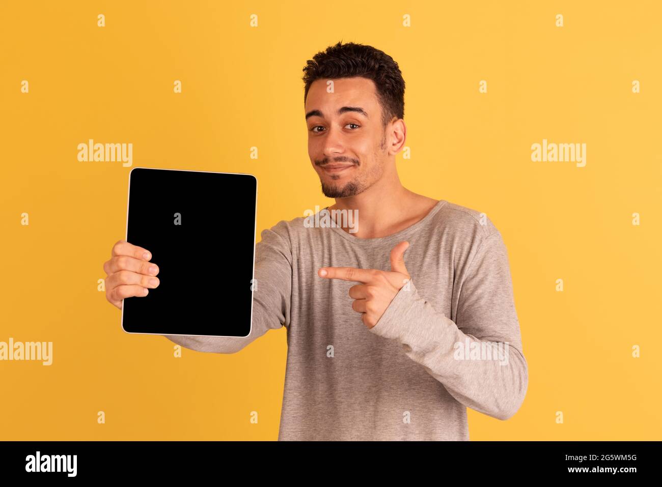Pointing on tablet. Caucasian man's portrait isolated on yellow ...