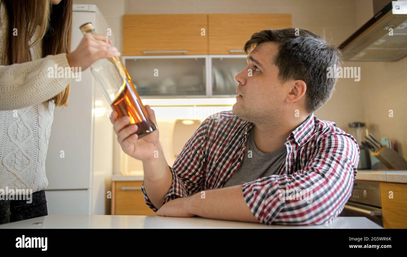 Young woman taking bottle of alcohol from male alcoholic drinking ...