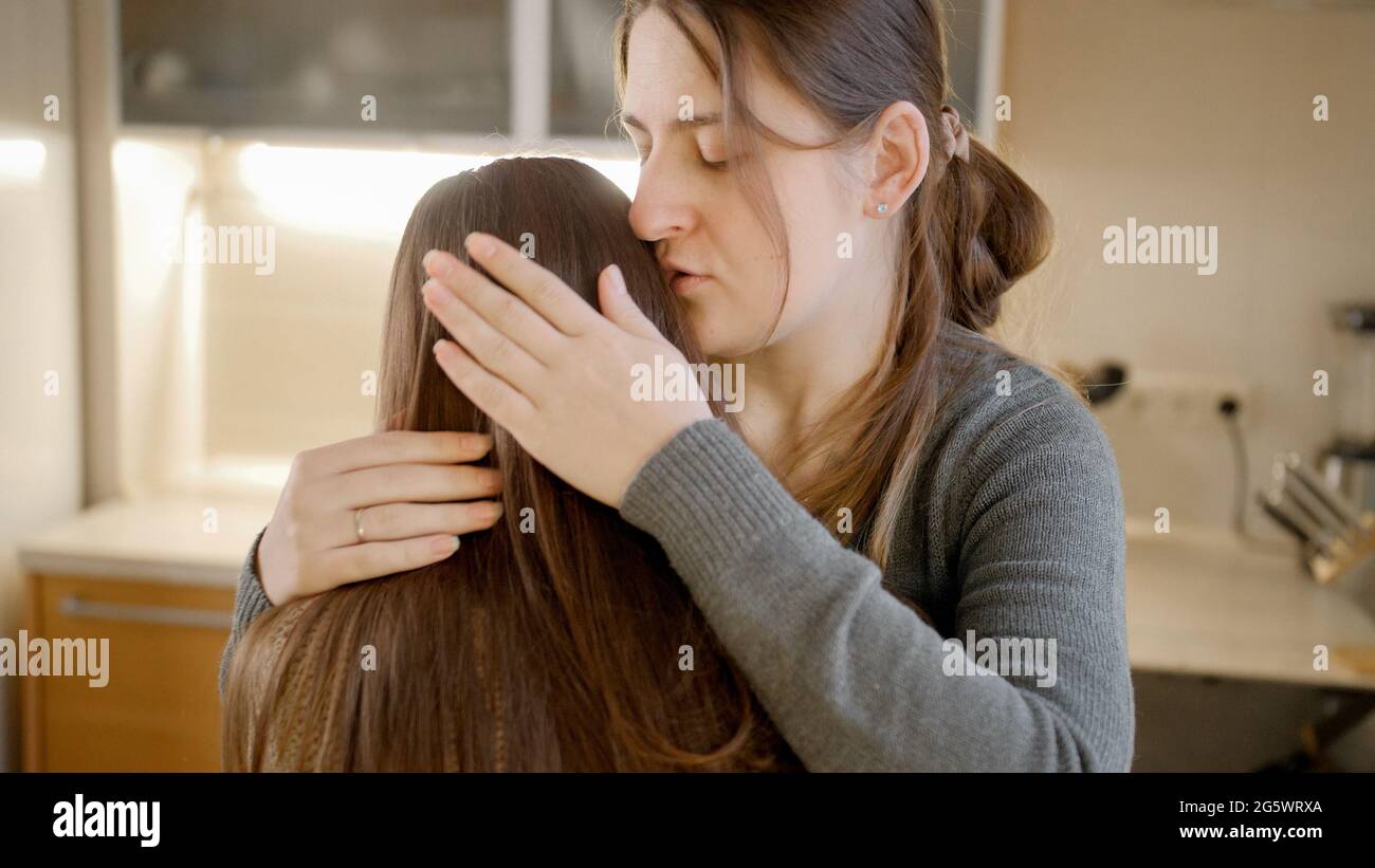 Young mother kissing and hugging upset crying daughter after talking about problems. Parent ...