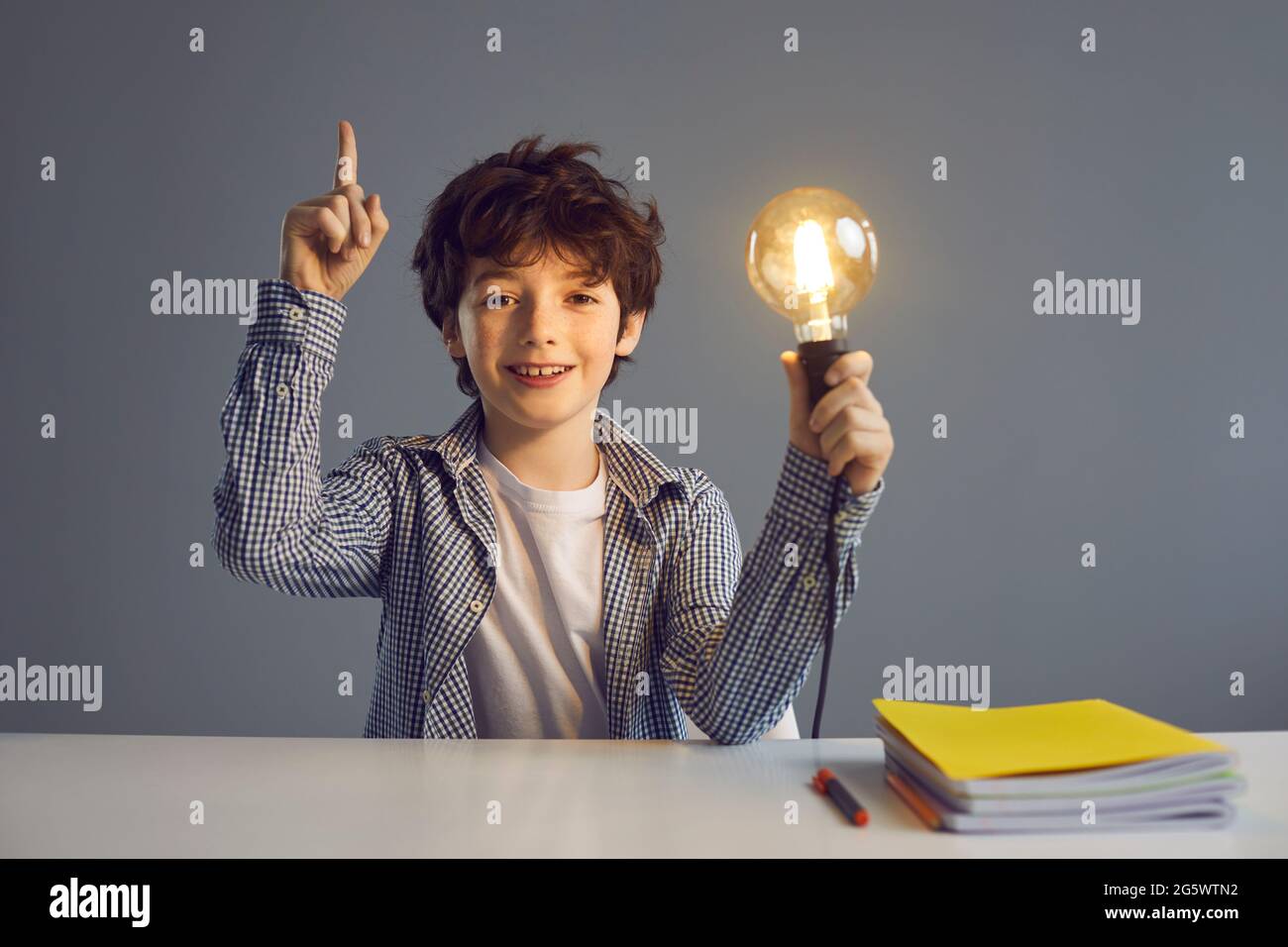 Portrait of a smart boy who holds a bright light bulb and raises his ...