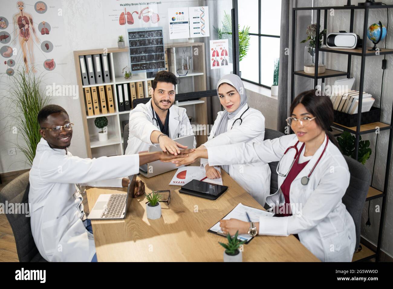 Team of multiracial medical specialists in white lab coats stacking ...