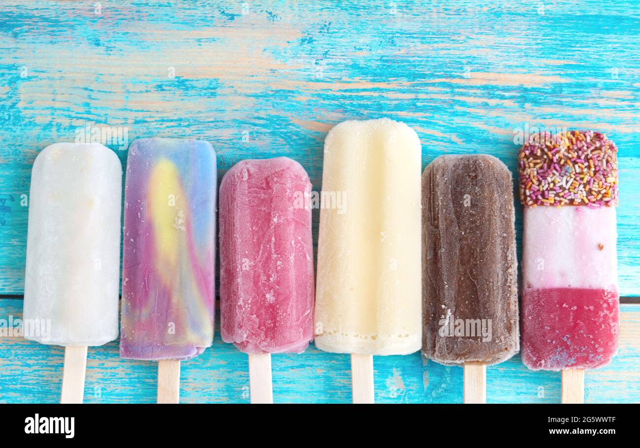 Assorted fruit and chocolate flavoured ice lolly sticks on wooden ...