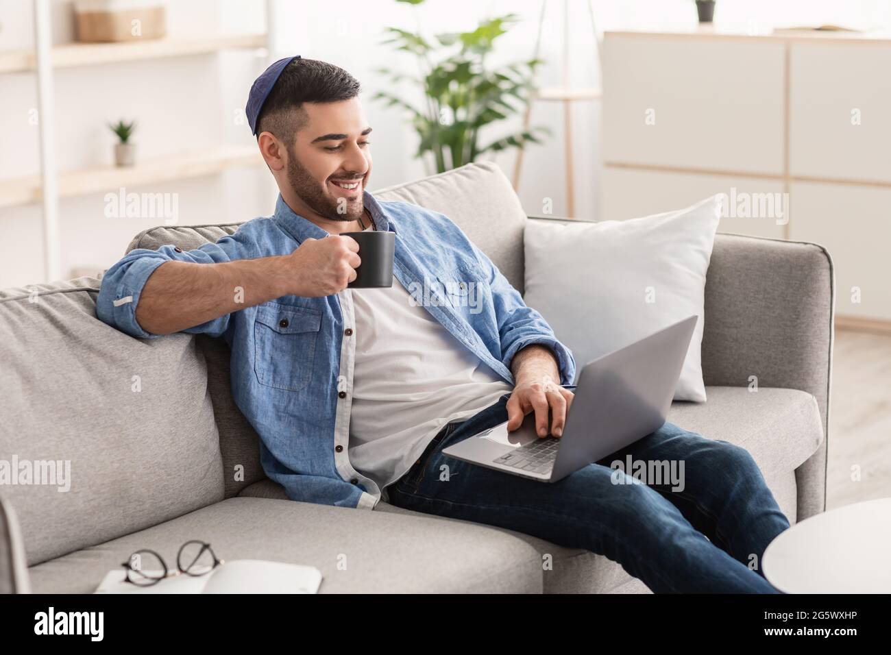 Smiling jewish man watching video on computer, drinking hot coffee ...
