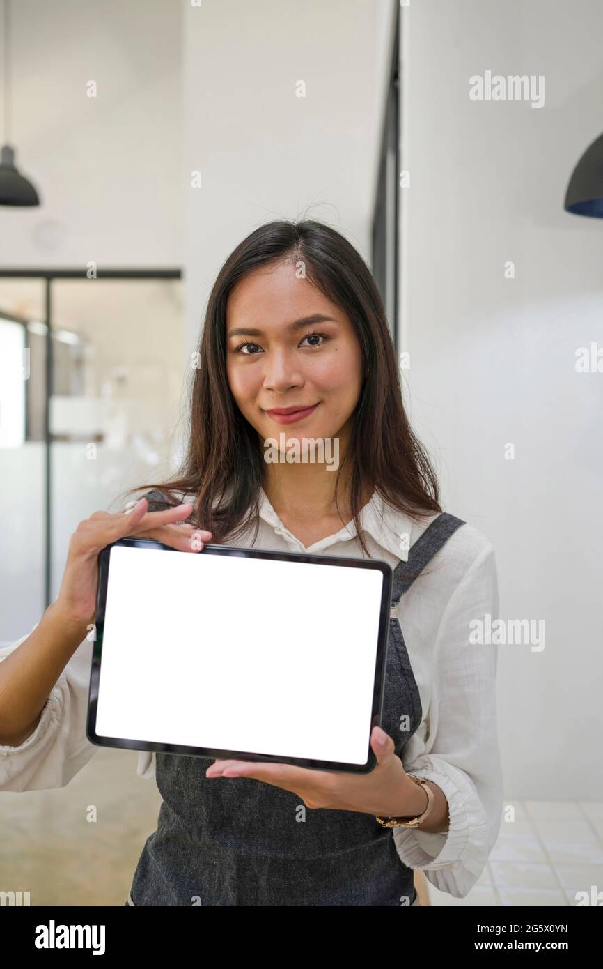 Cheerful young female owner showing digital tablet while standing in ...