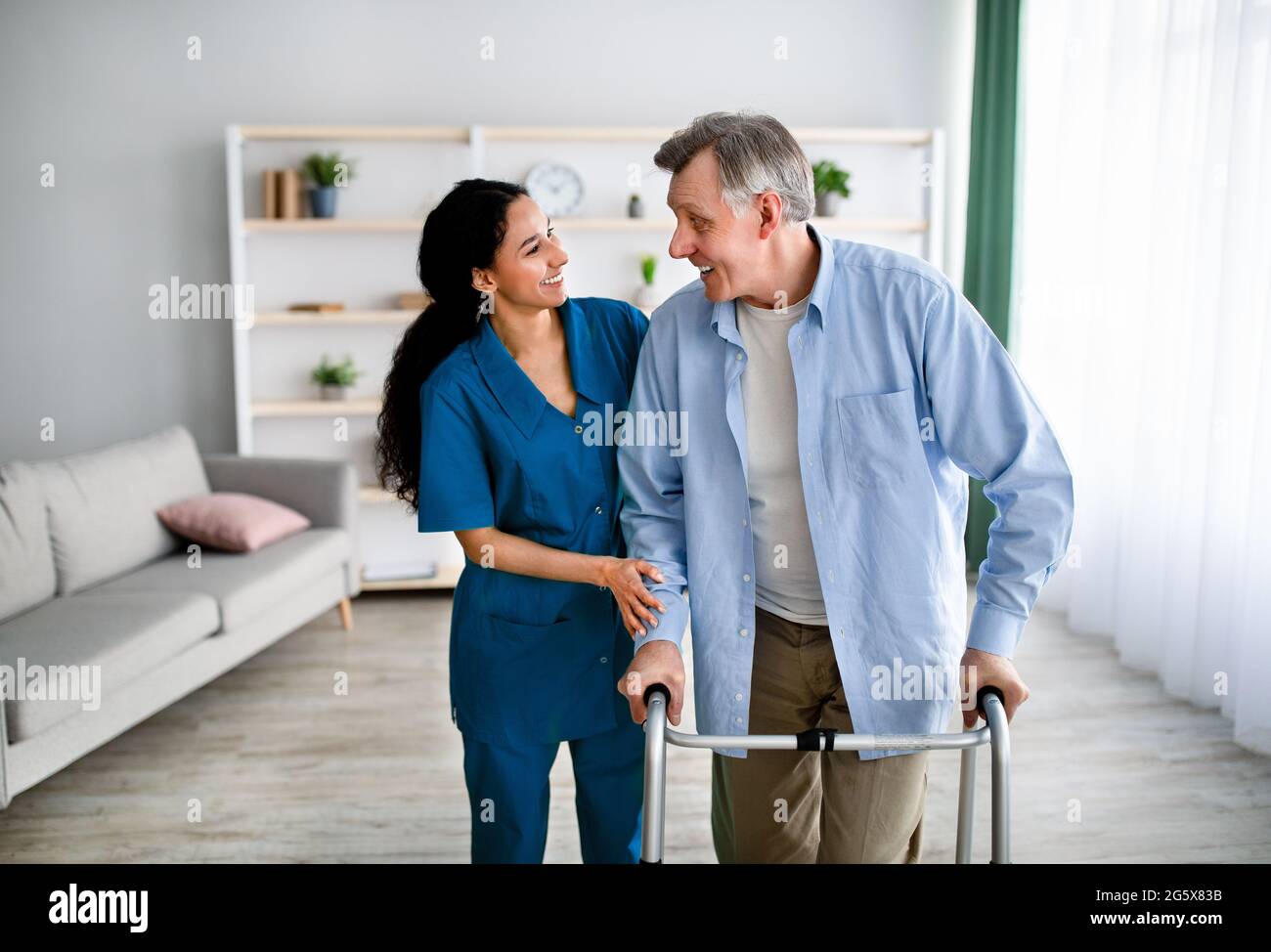 Female Caregiver Assisting Elderly Man To Walk With Frame At Home