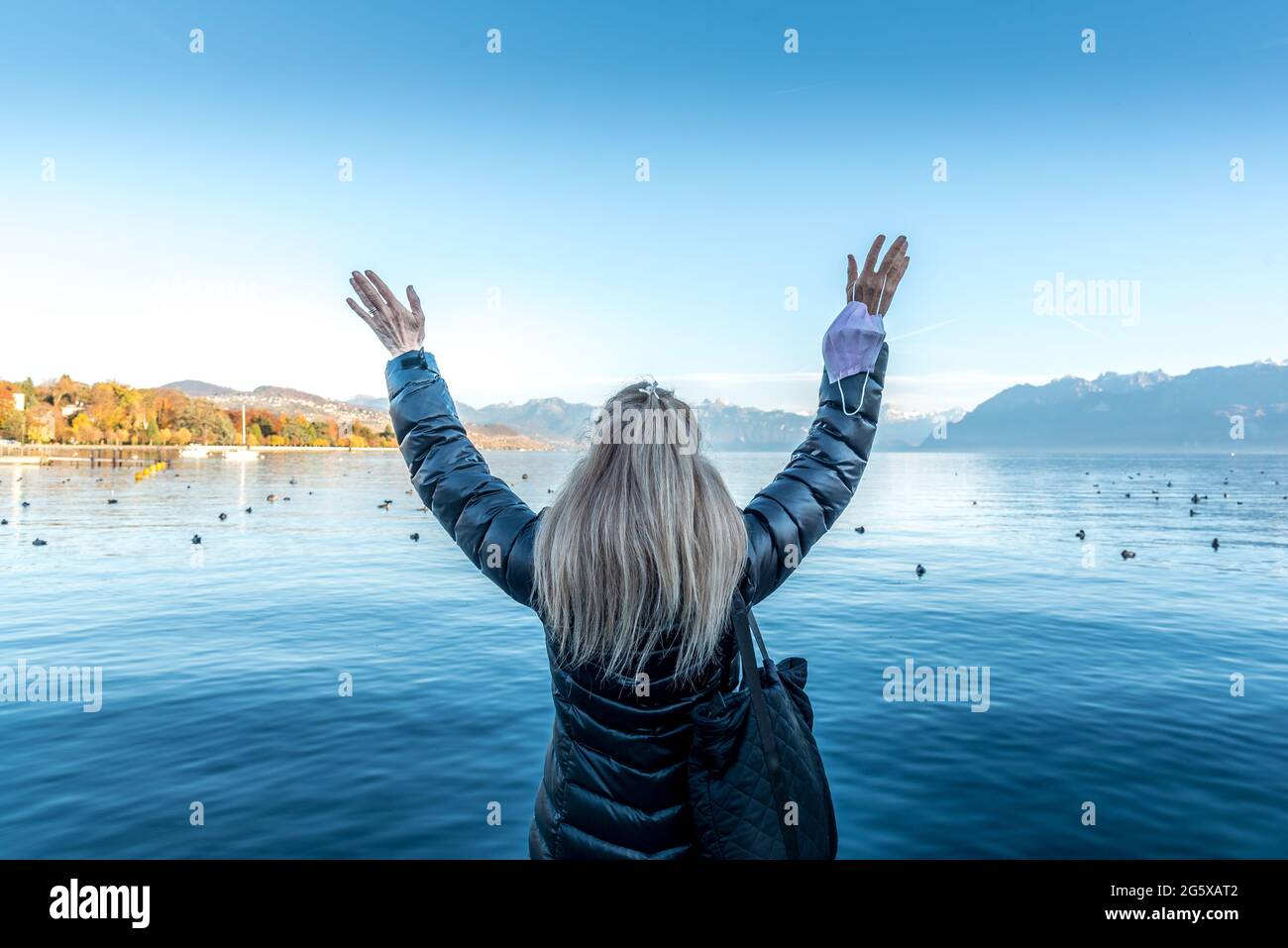 Faceless blonde woman in a lake raising her arms and holding her face ...
