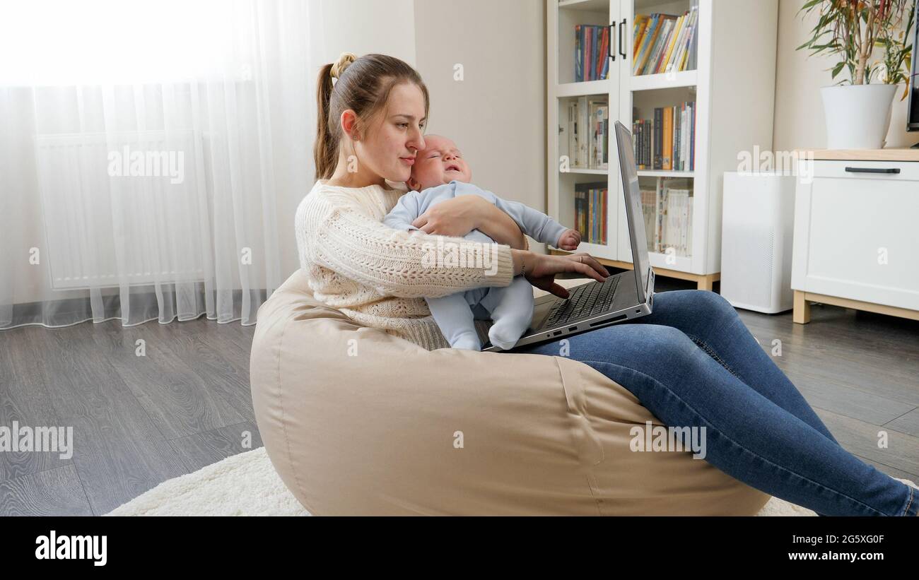 Crying baby sitting on mothers lap while she is working from home on ...