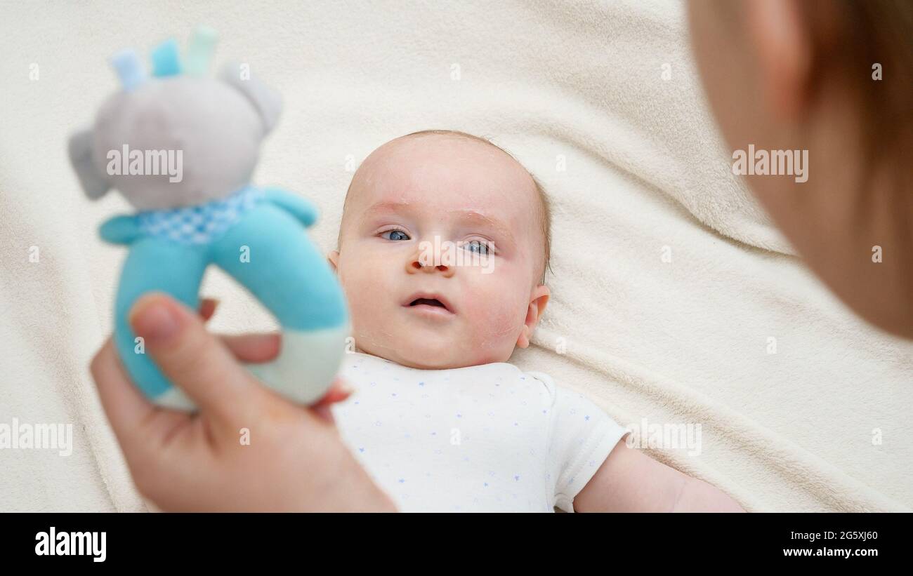 Young mother talking to her little baby in bed and shaking colorful ...