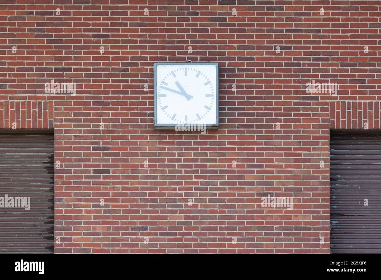 A clock hangs on a brick wall and a part of a lowered brown roller ...