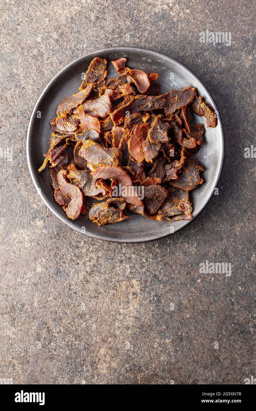 Sliced beef jerky. Dried beef meat on plate on old kitchen table. Top ...