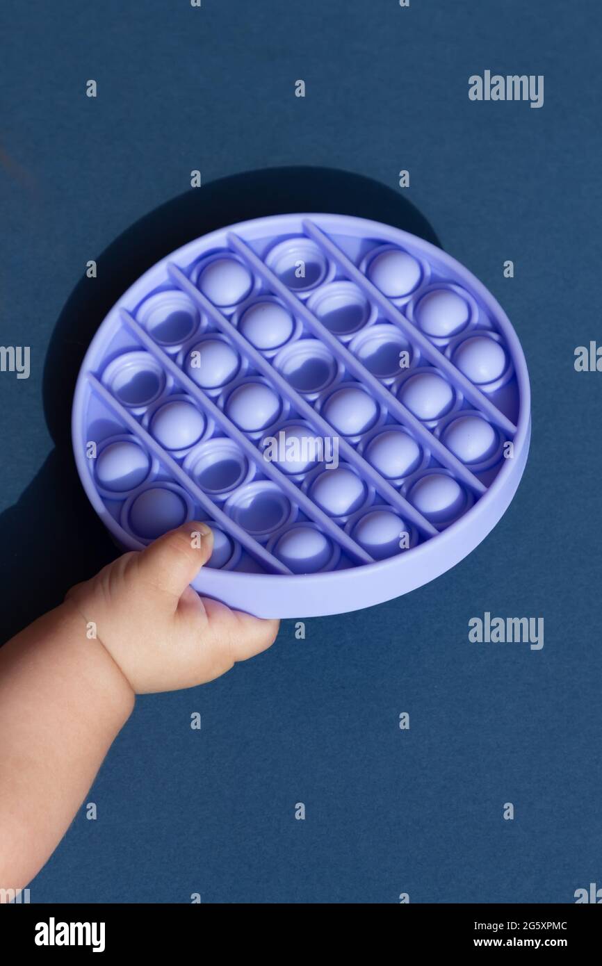 Children's hand is playing with a purple popit toy on a blue background ...