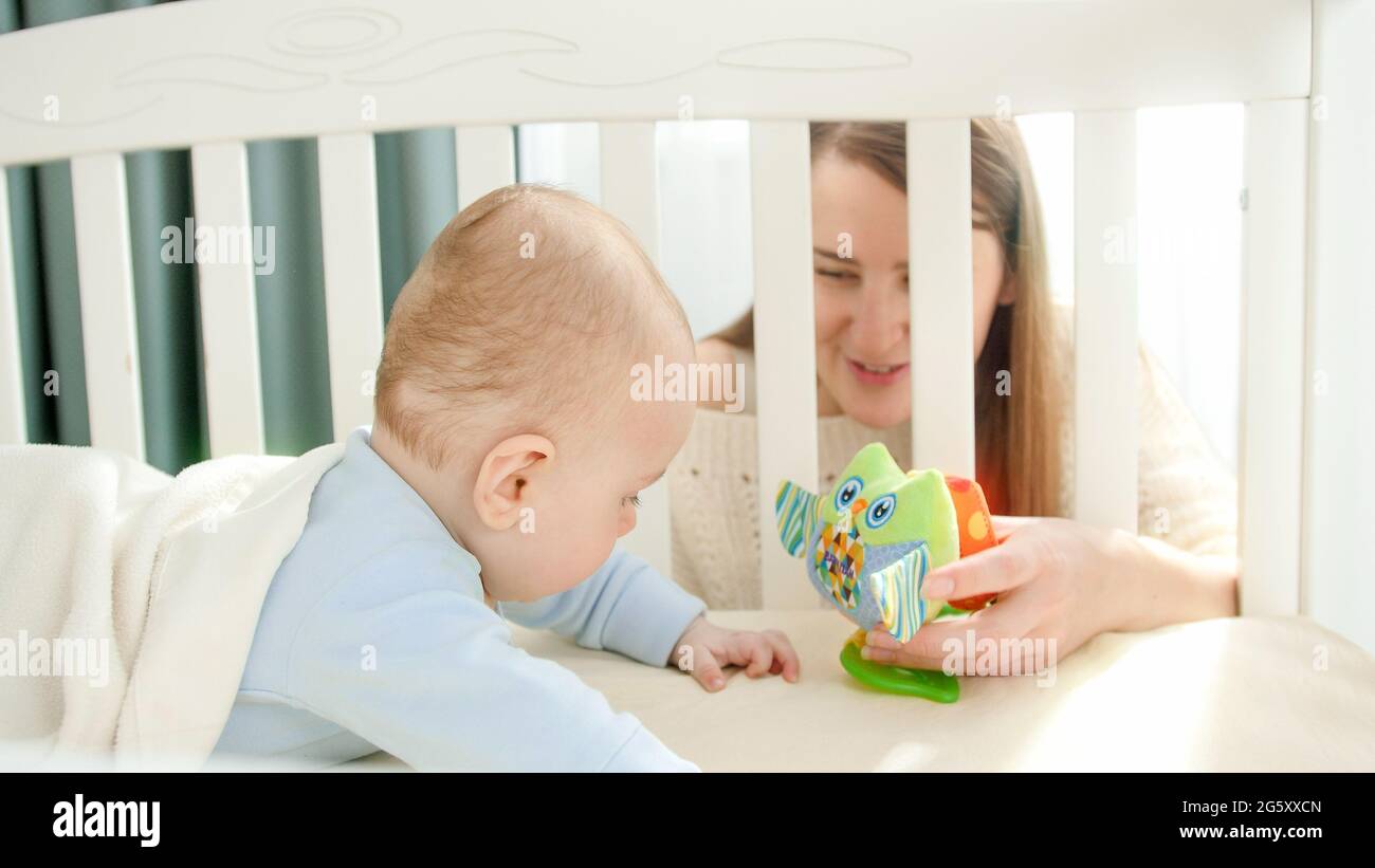 Mother sitting at cradle and giving toy to her baby son . Concept of ...