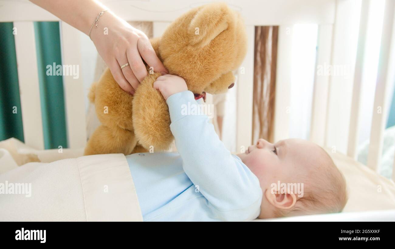 Adorable baby boy reaching and playing with toy teddy bear in cradle ...