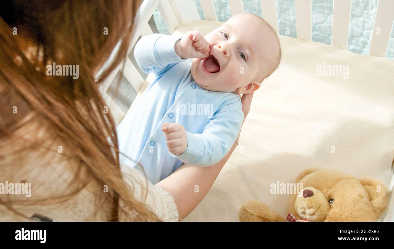 Young mother holding and rocking her smiling cute baby son in cradle ...