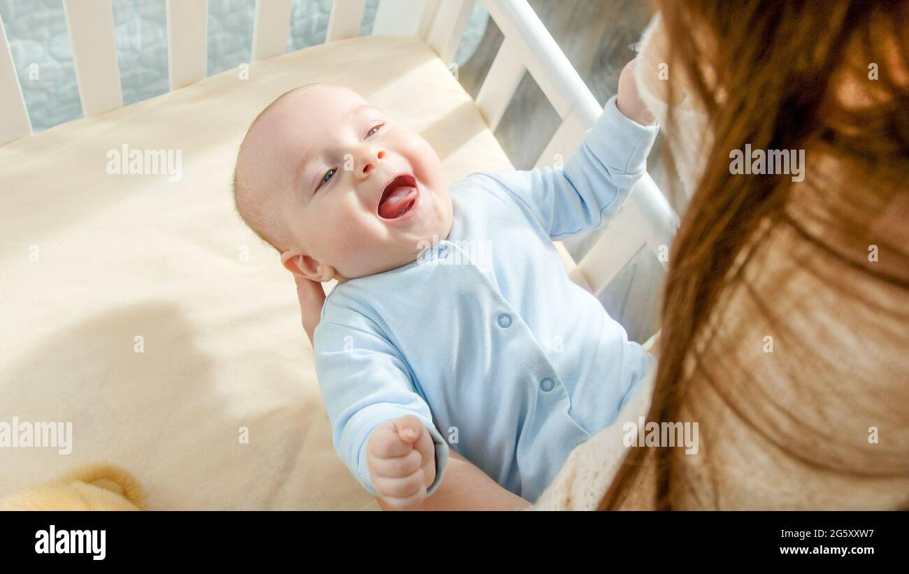 Happy smiling baby boy looking at mother rocking him in cradle. Concept ...