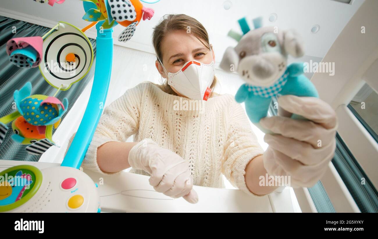 Mother in medical respirator mask playing toys with her baby lying in ...