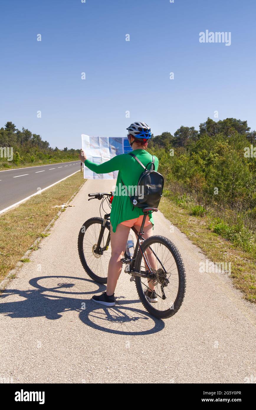 tourist girl in a helmet on a bicycle examining a map at the ...