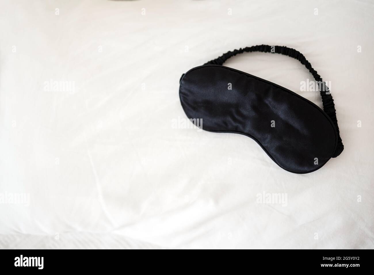 Black satin-silk sleep mask on white bed linen background, no people ...