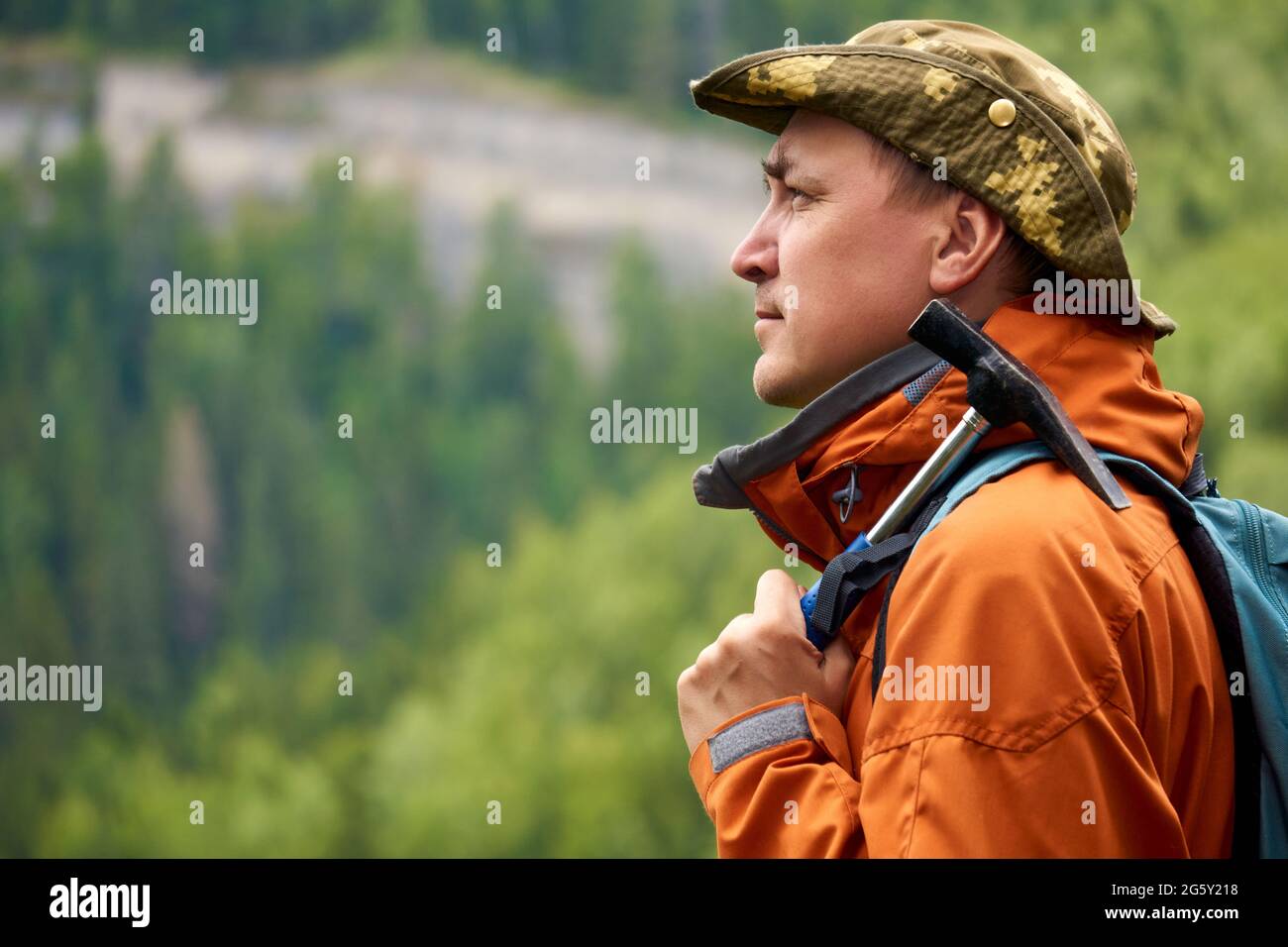 male geologist with a backpack and a geological hammer in hand against ...