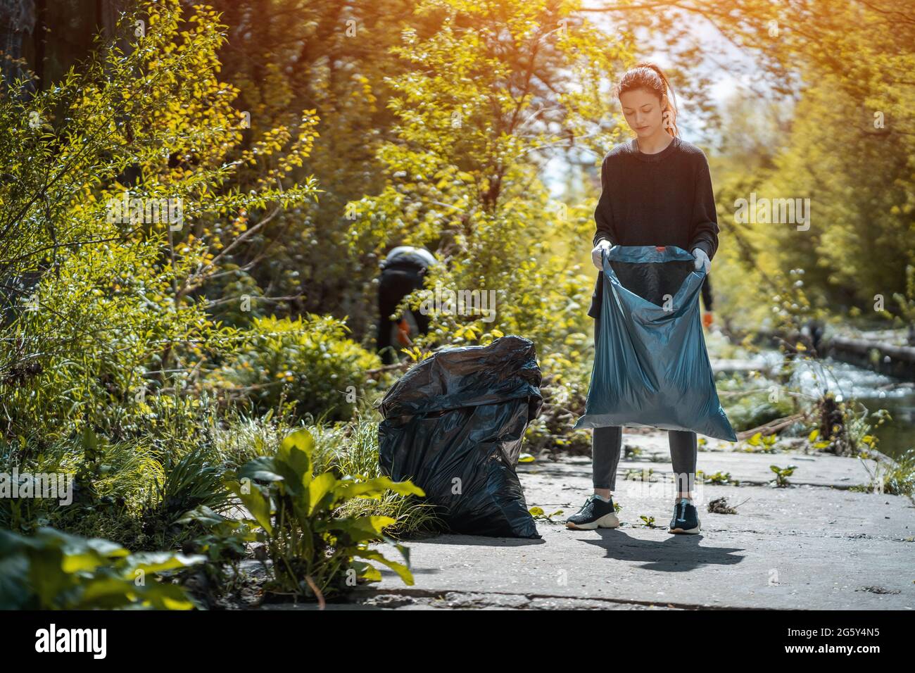 volunteer female cleaning up park and tree from plastic litter with ...