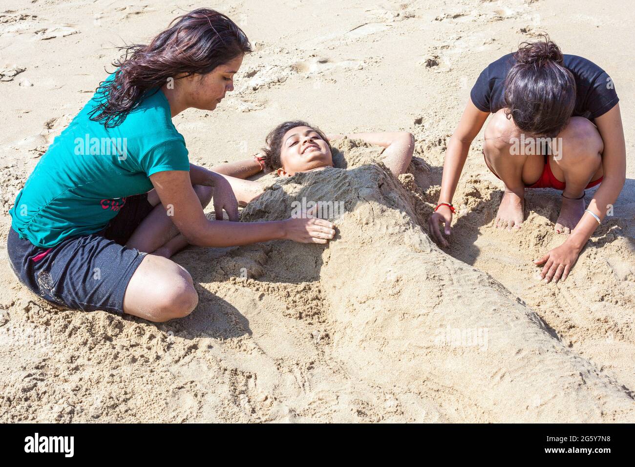 Attractive Indian females bury their pretty friend in the sand on the ...
