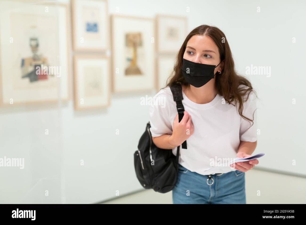 Interested girl in a protective mask in the art gallery studies the ...