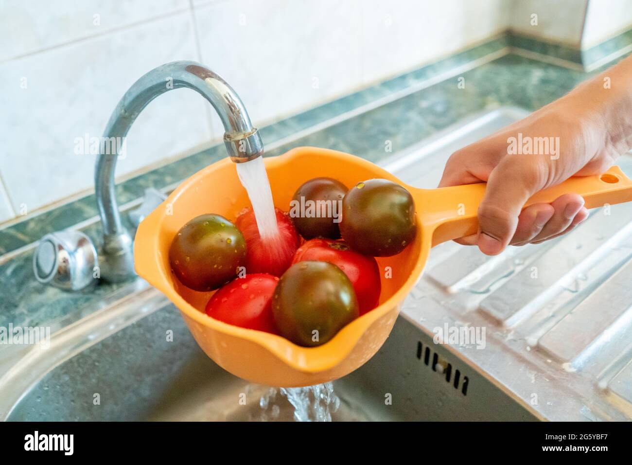hand holding a colander with fresh fruit and berries and washing it in ...