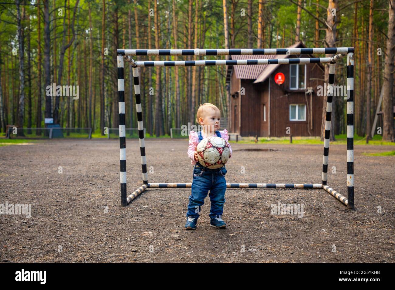 little active girl baby blond playing with football ball in the forest ...