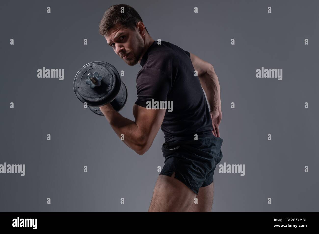 Muscular young bodybuilder doing bicep curl with dumbbell Stock Photo ...