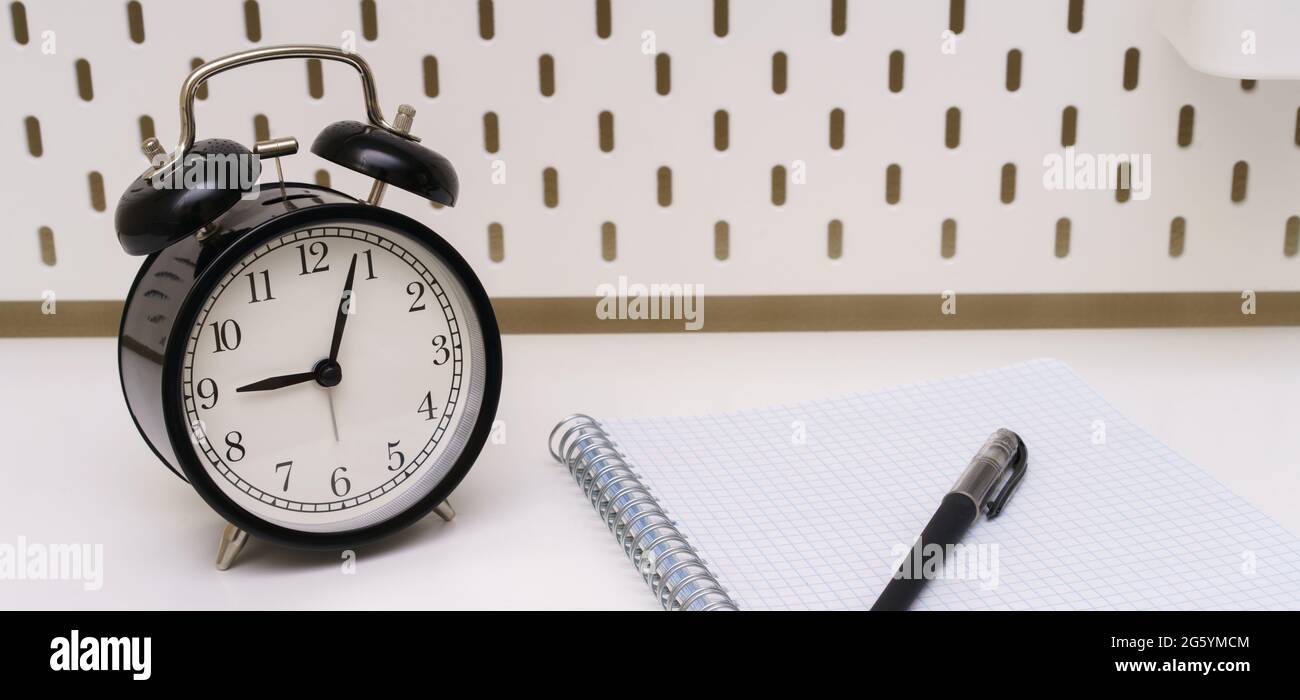 a black alarm clock, notepad, pen are placed on a white background of ...