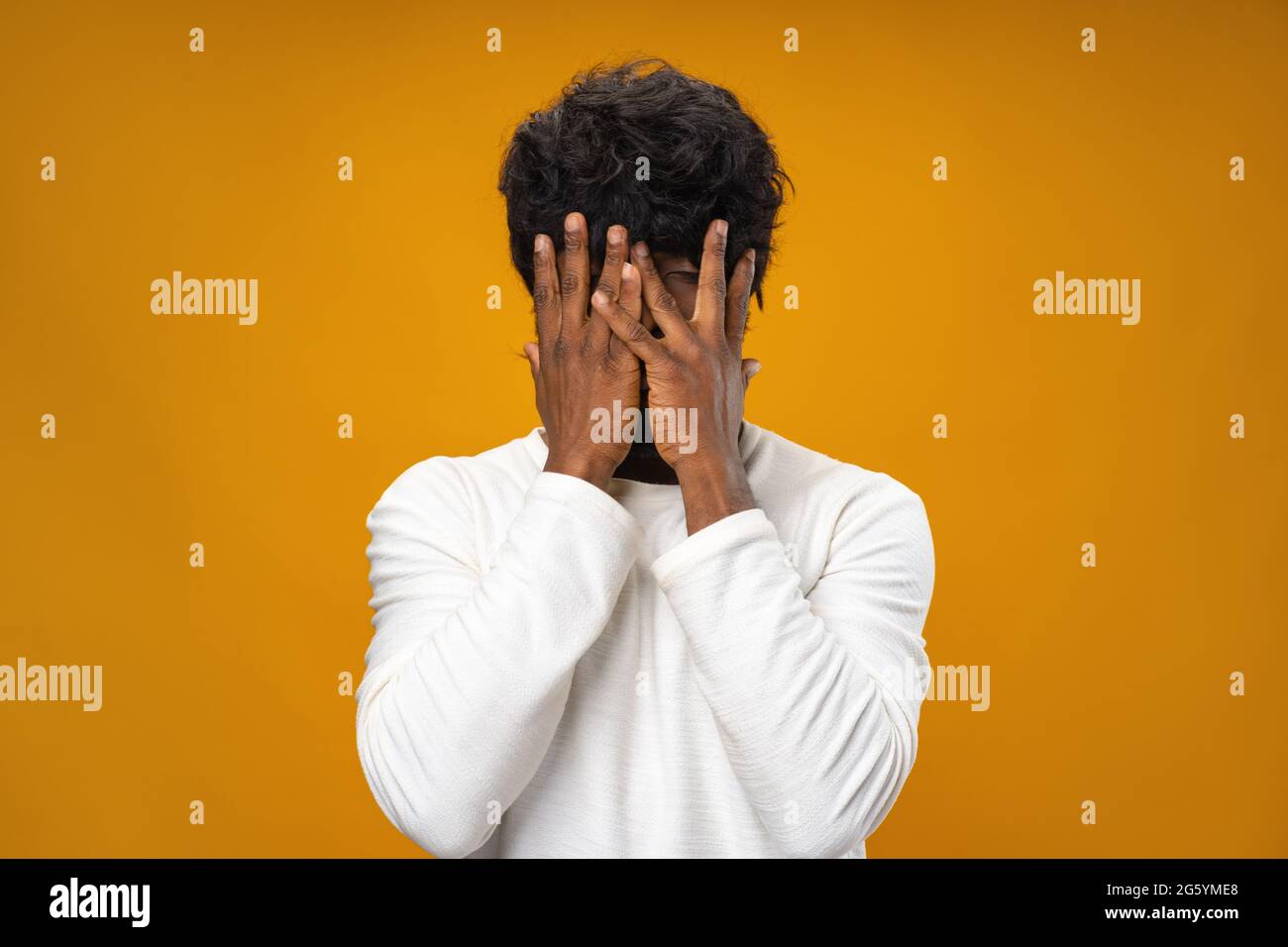 Black man closing face with hands against yellow background Stock Photo ...
