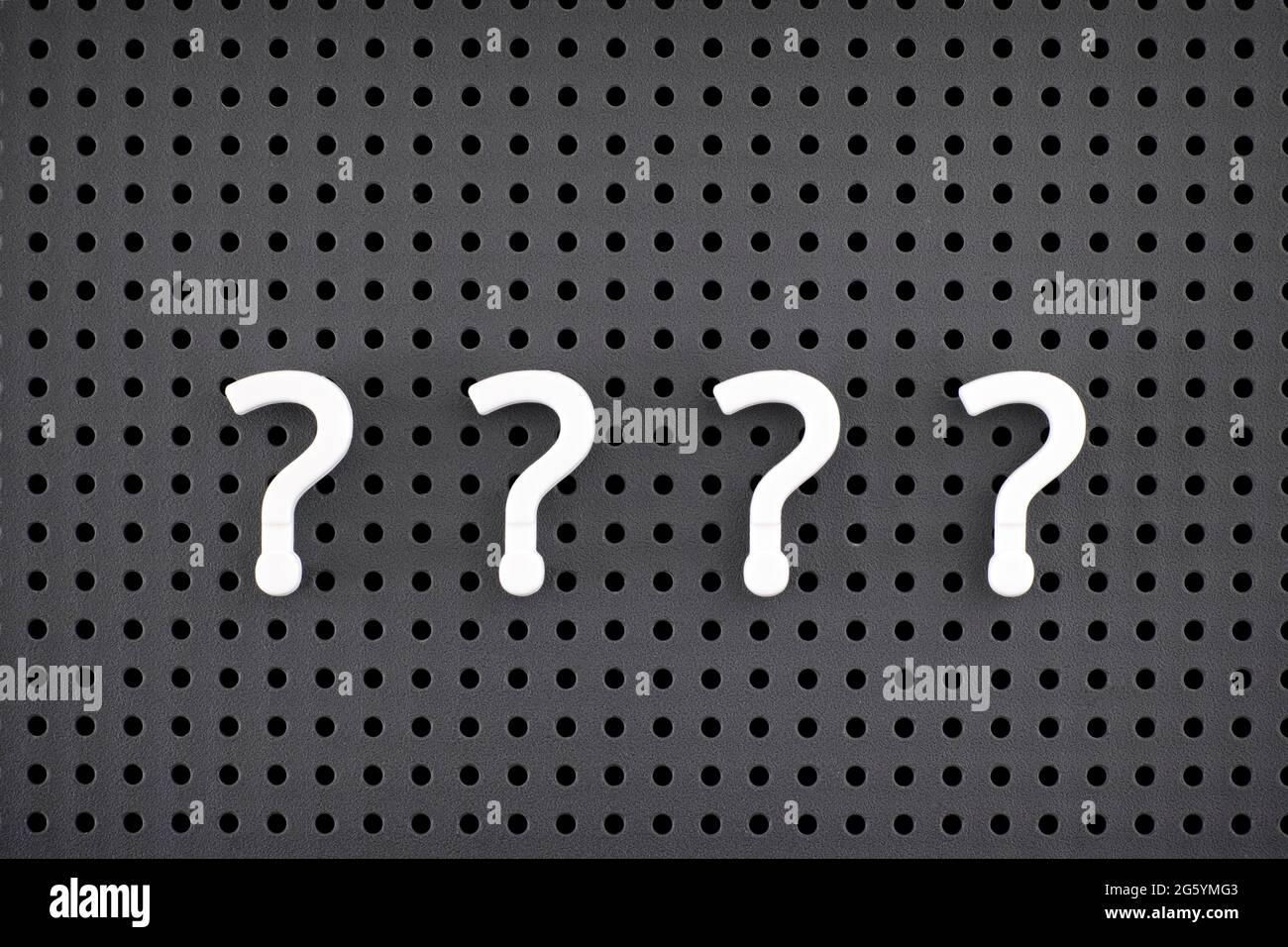 Four question marks spelled out by white symbol on a gray pegboard ...