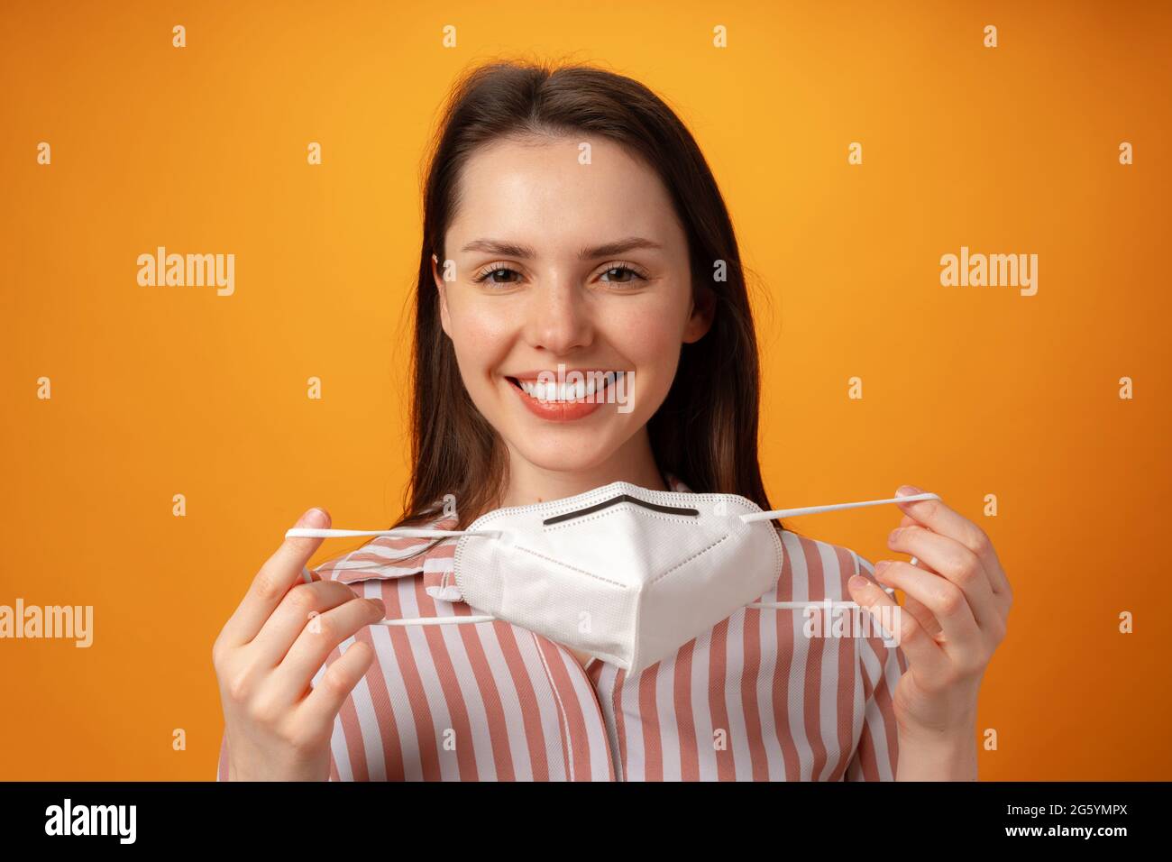 Studio portrait of a young woman taking off her face mask against ...