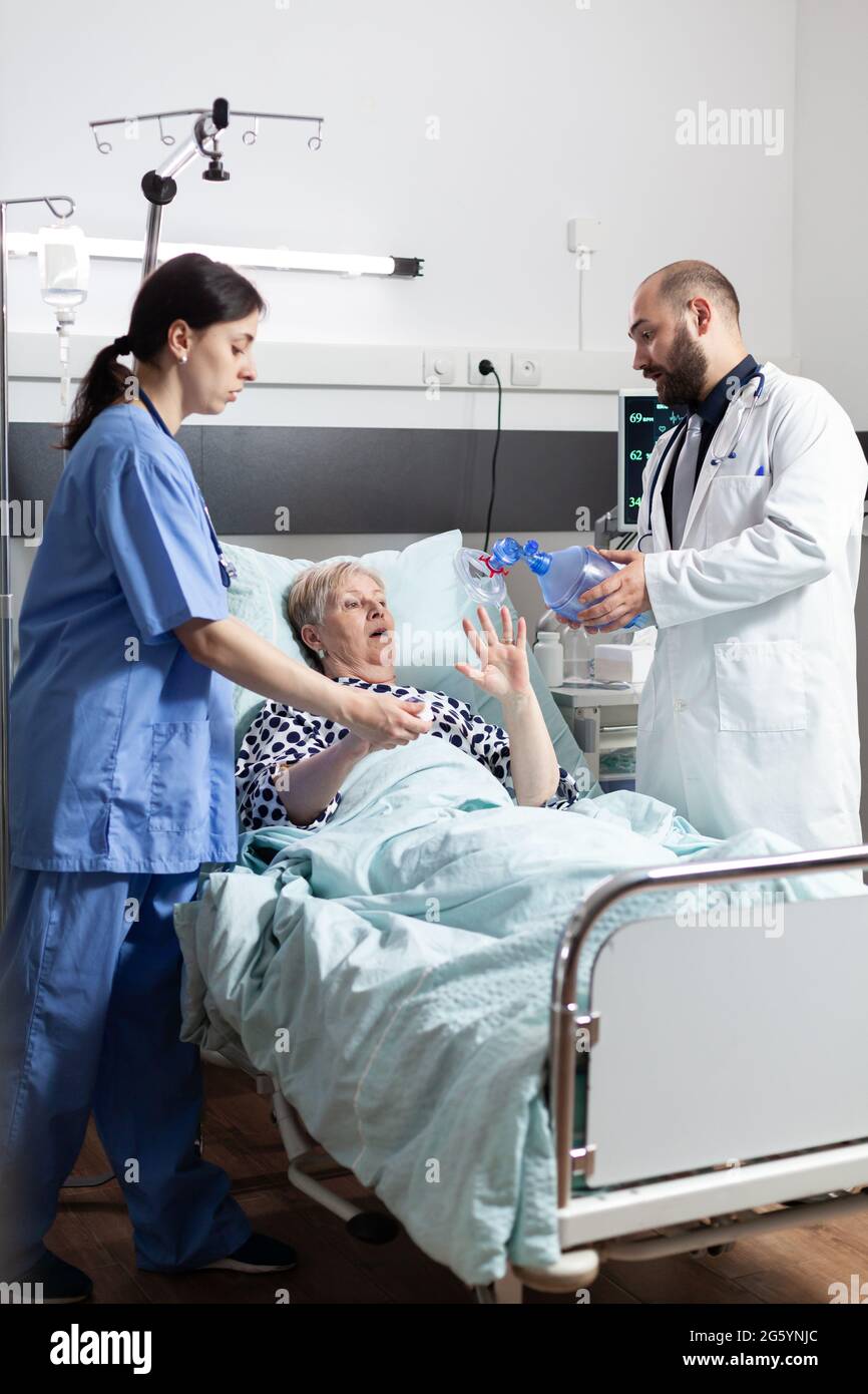 Medical team helping senior woman patient laying in hospital bed, to ...