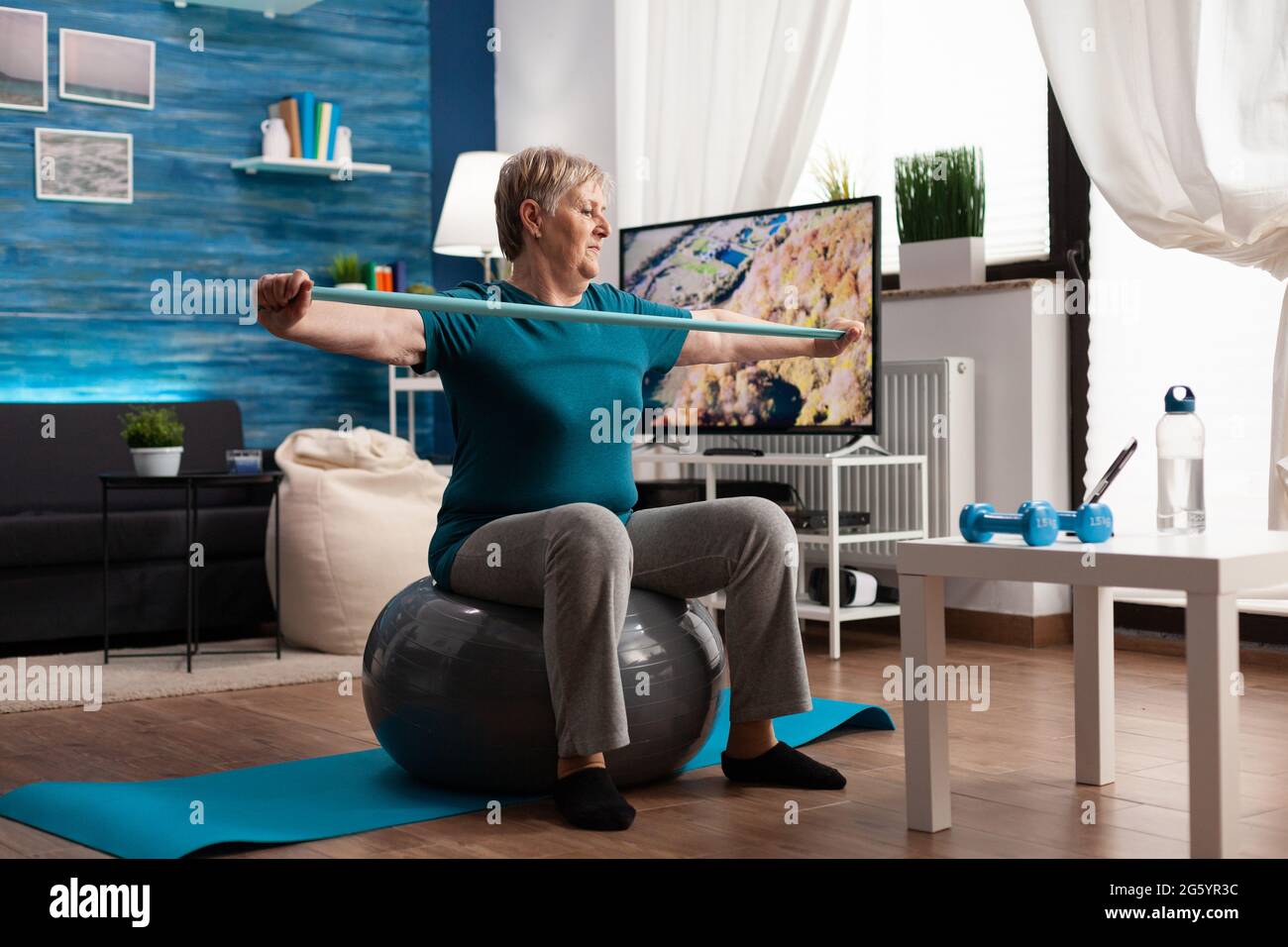 Cheerful retired pensioner working arm muscles using elastic band ...