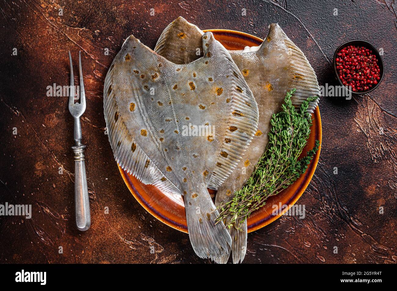 Raw flounder or plaice on rustic plate with herbs. Dark background. Top ...