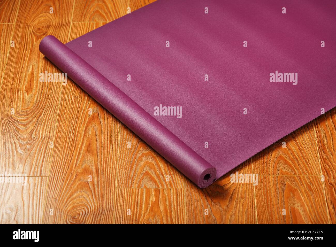 An unfolded lilac-colored yoga mat is unfolded on the wooden floor. Top ...