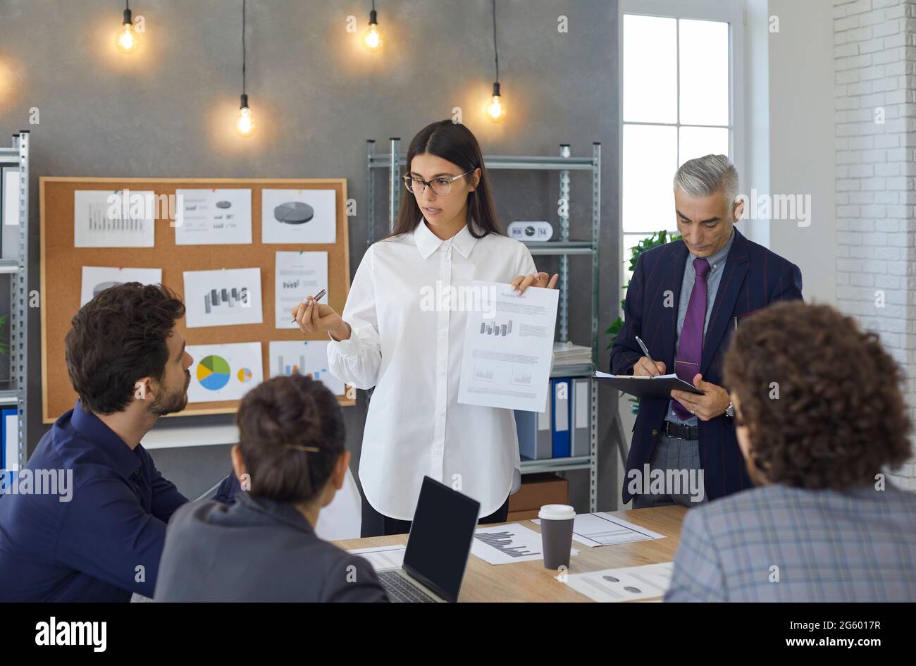 Young woman presenting her report to a team of colleagues in a ...