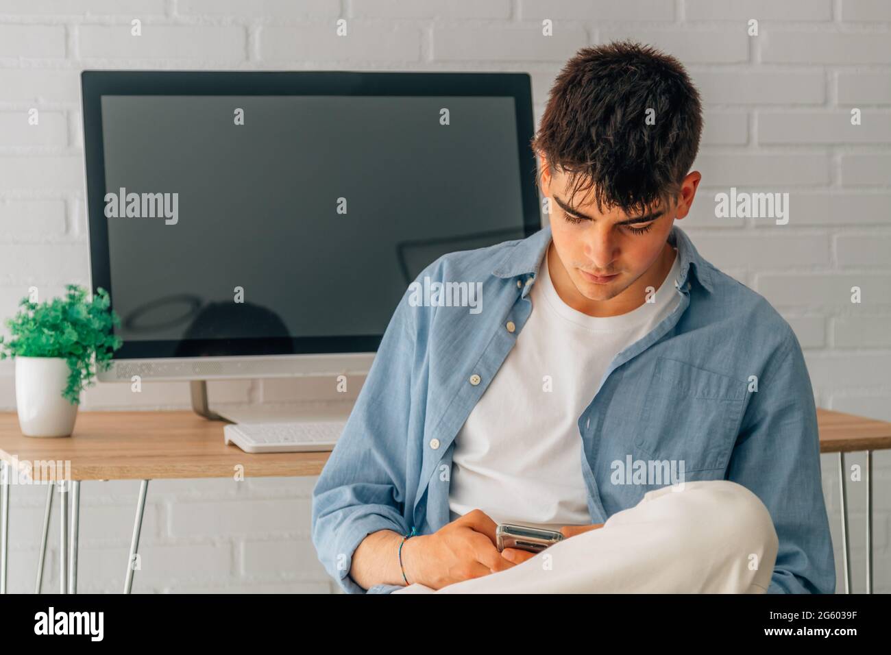 student at home with mobile phone and desk with computer behind Stock ...