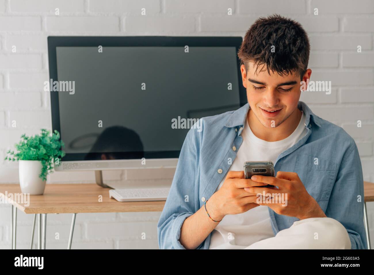 student at home with mobile phone and desk with computer behind Stock ...