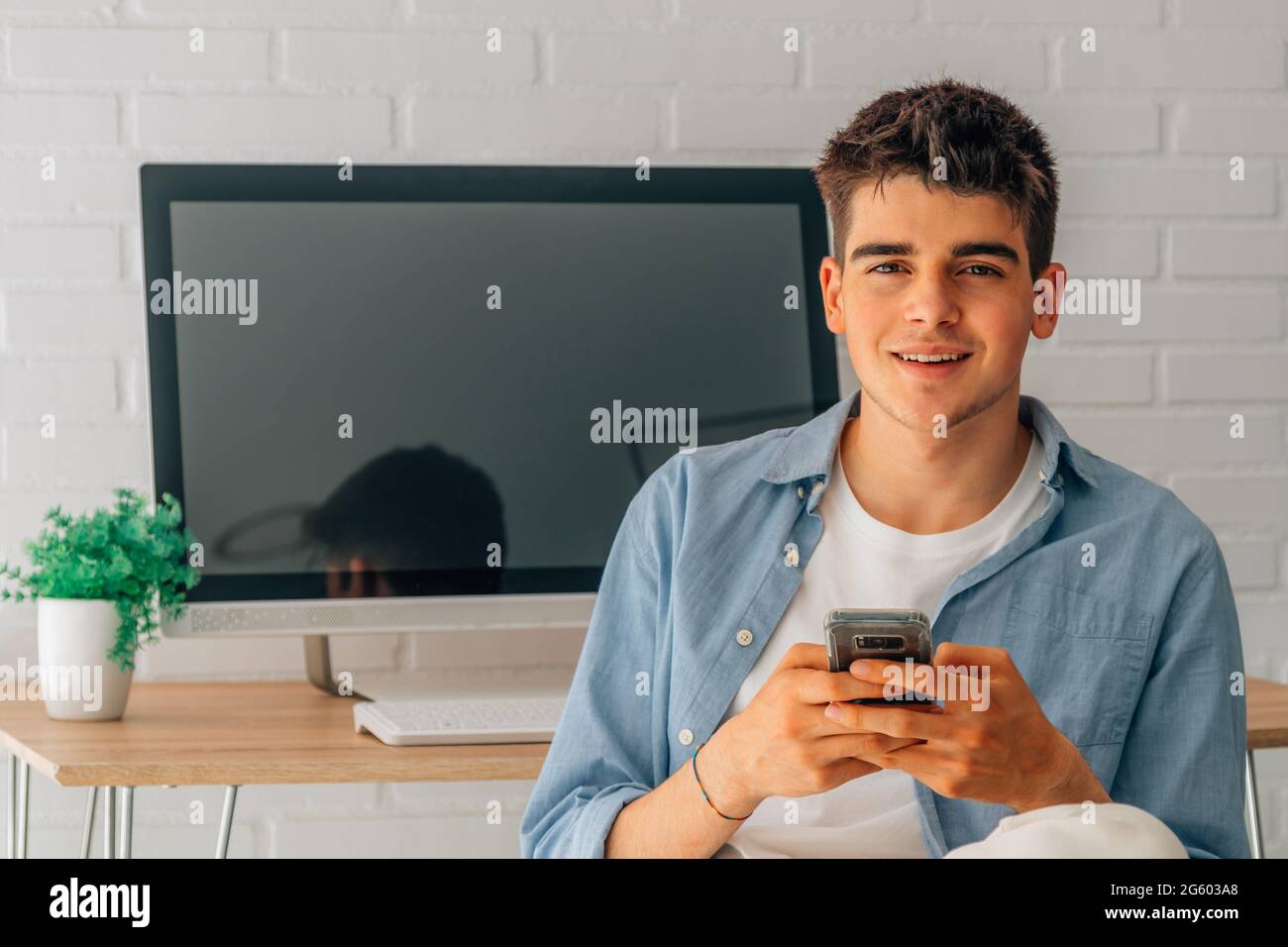 student at home with mobile phone and desk with computer behind Stock ...