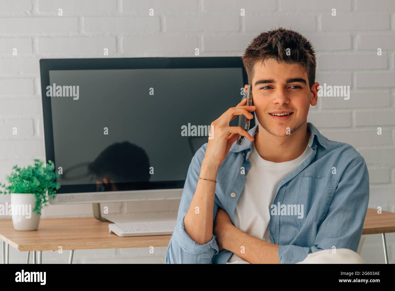 student at home with mobile phone and desk with computer behind Stock ...