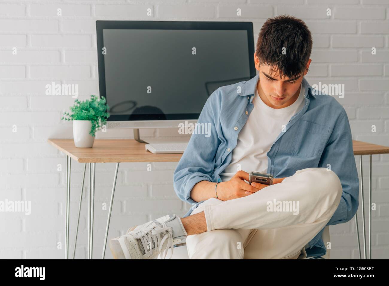 student at home with mobile phone and desk with computer behind Stock ...