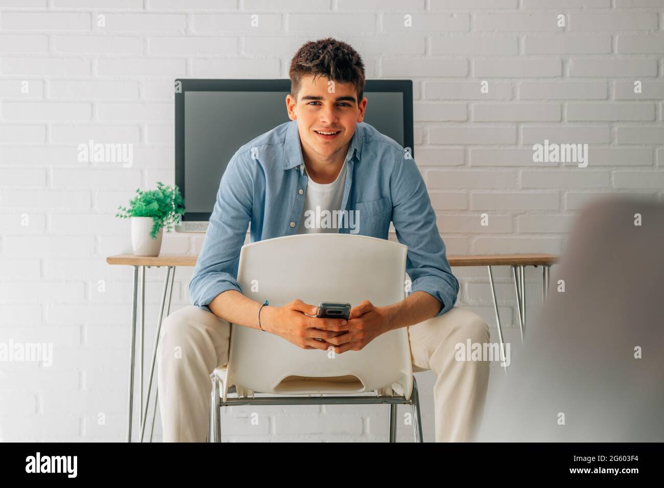 student at home with mobile phone and desk with computer behind Stock ...