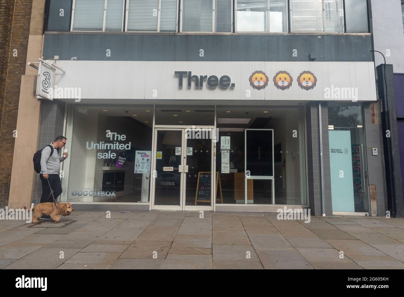 London, UK. 1st July, 2021. A man with his dog walk past the Three shop ...