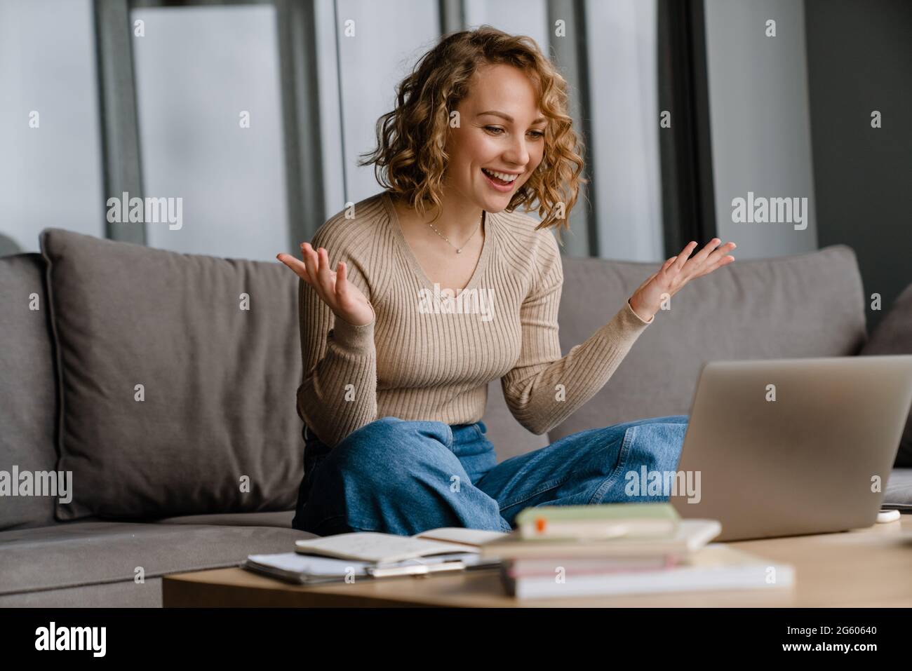 Young white woman gesturing and using laptop while sitting on couch at ...