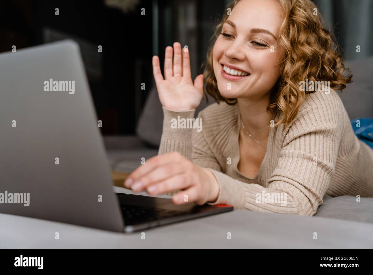 White blonde woman gesturing and using laptop while lying on couch at ...